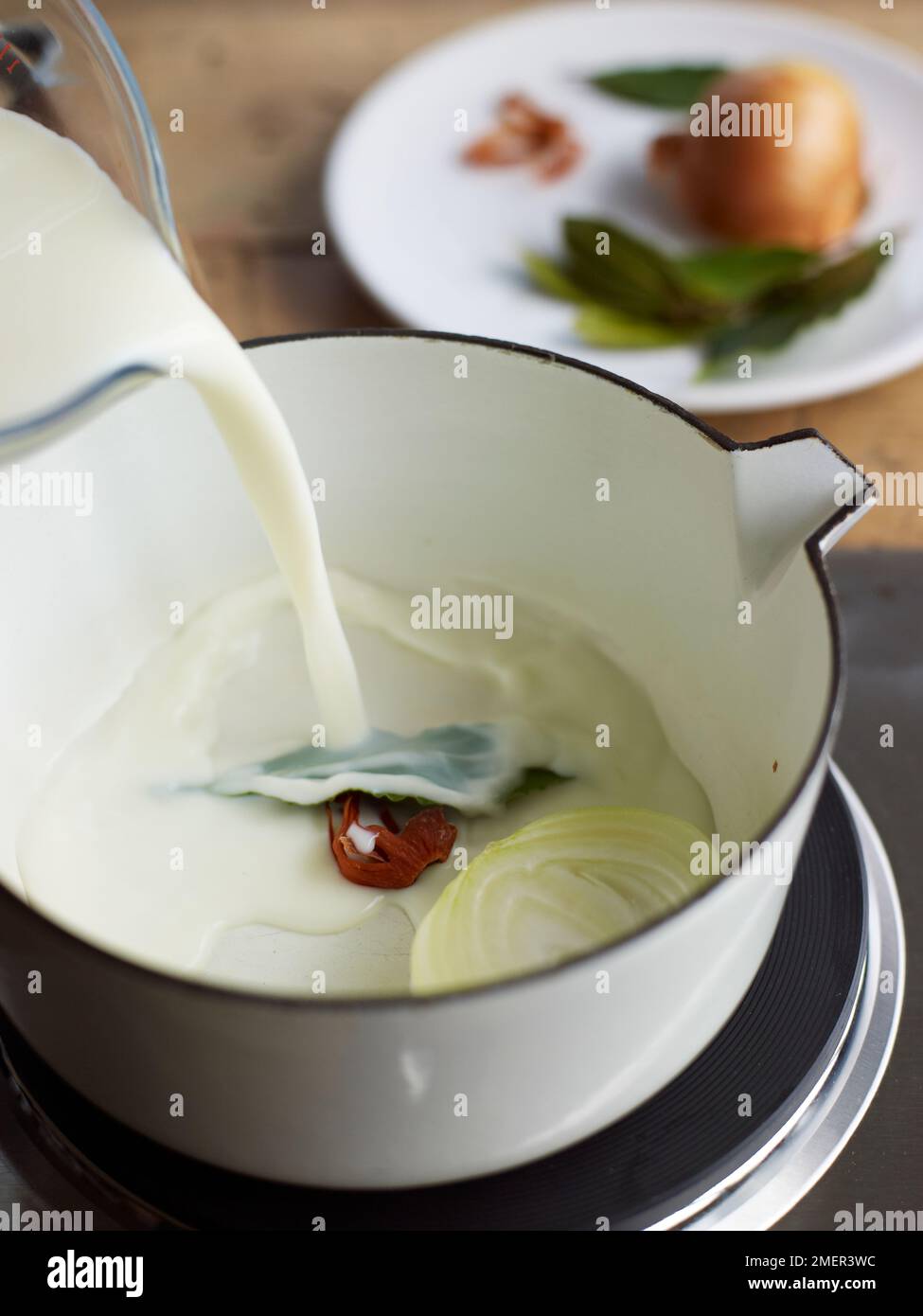 Pouring milk in pan with bay leaf, onion, and mace, to make infused ...