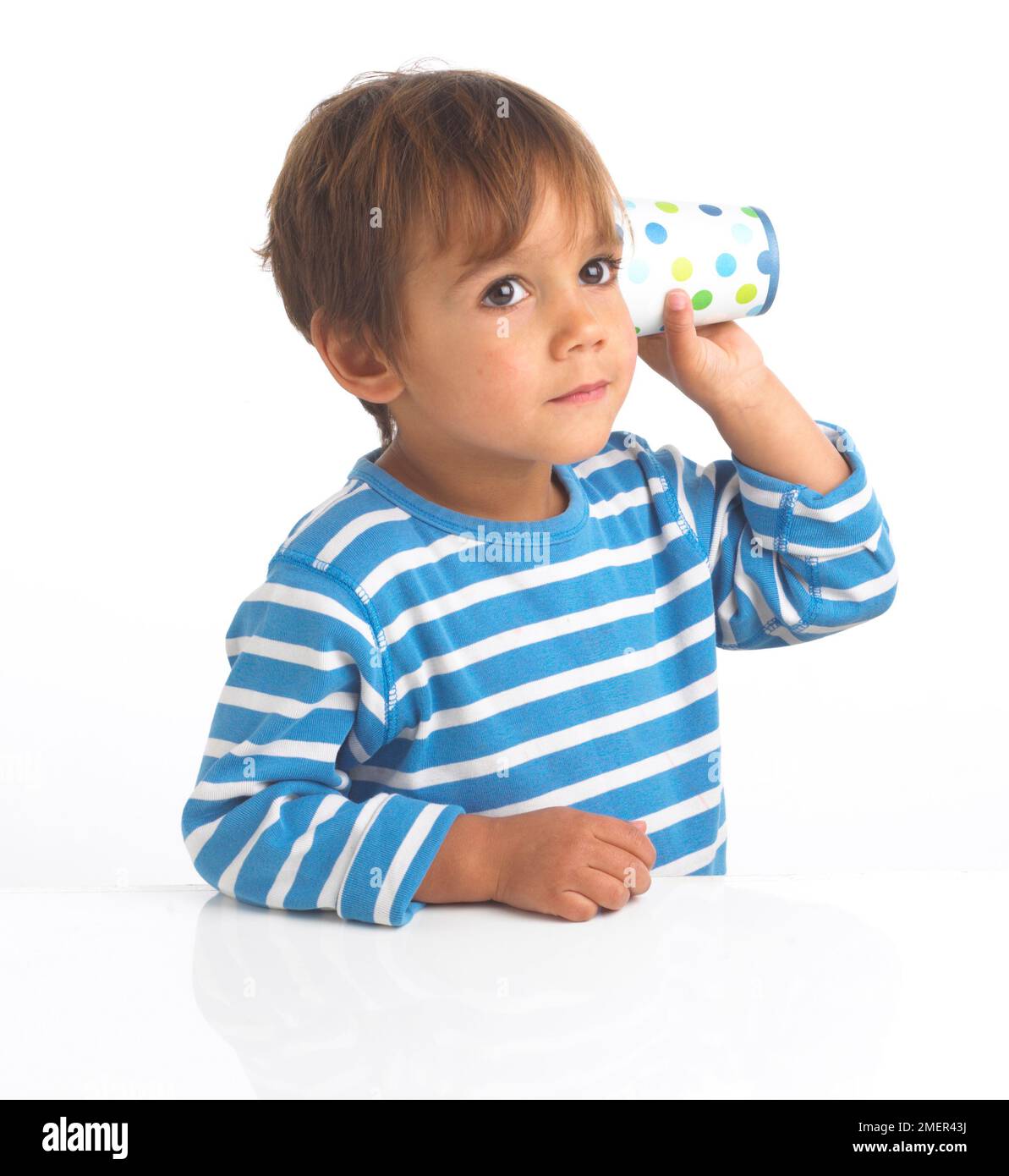 Boy wearing blue and white striped top holding spotty paper cup to his ...