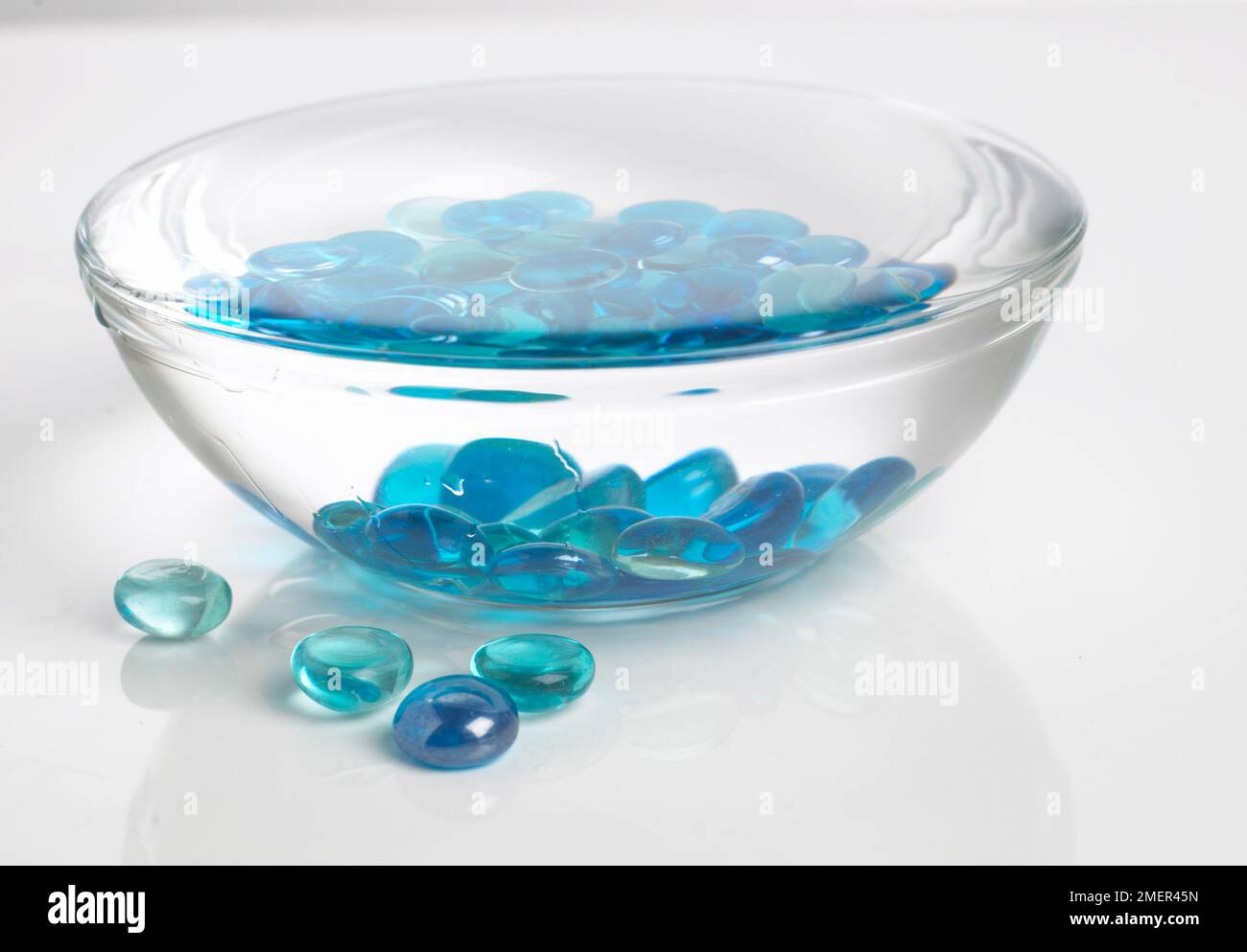 Blue glass pebbles in an overflowing bowl of water Stock Photo - Alamy