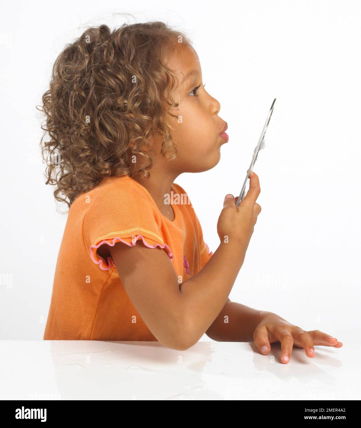 Girl wearing orange top blowing through metal bubble stick, side view ...