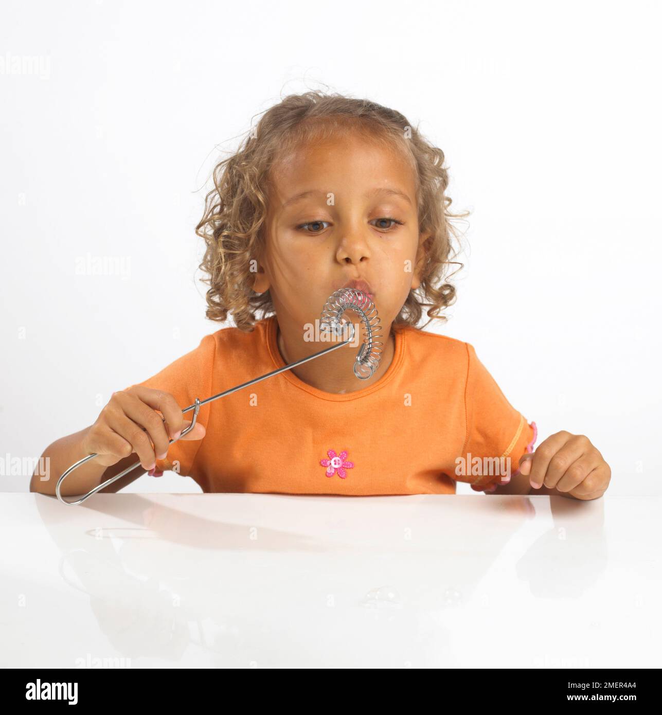 Girl wearing orange top blowing metal whisk, 4 years Stock Photo - Alamy