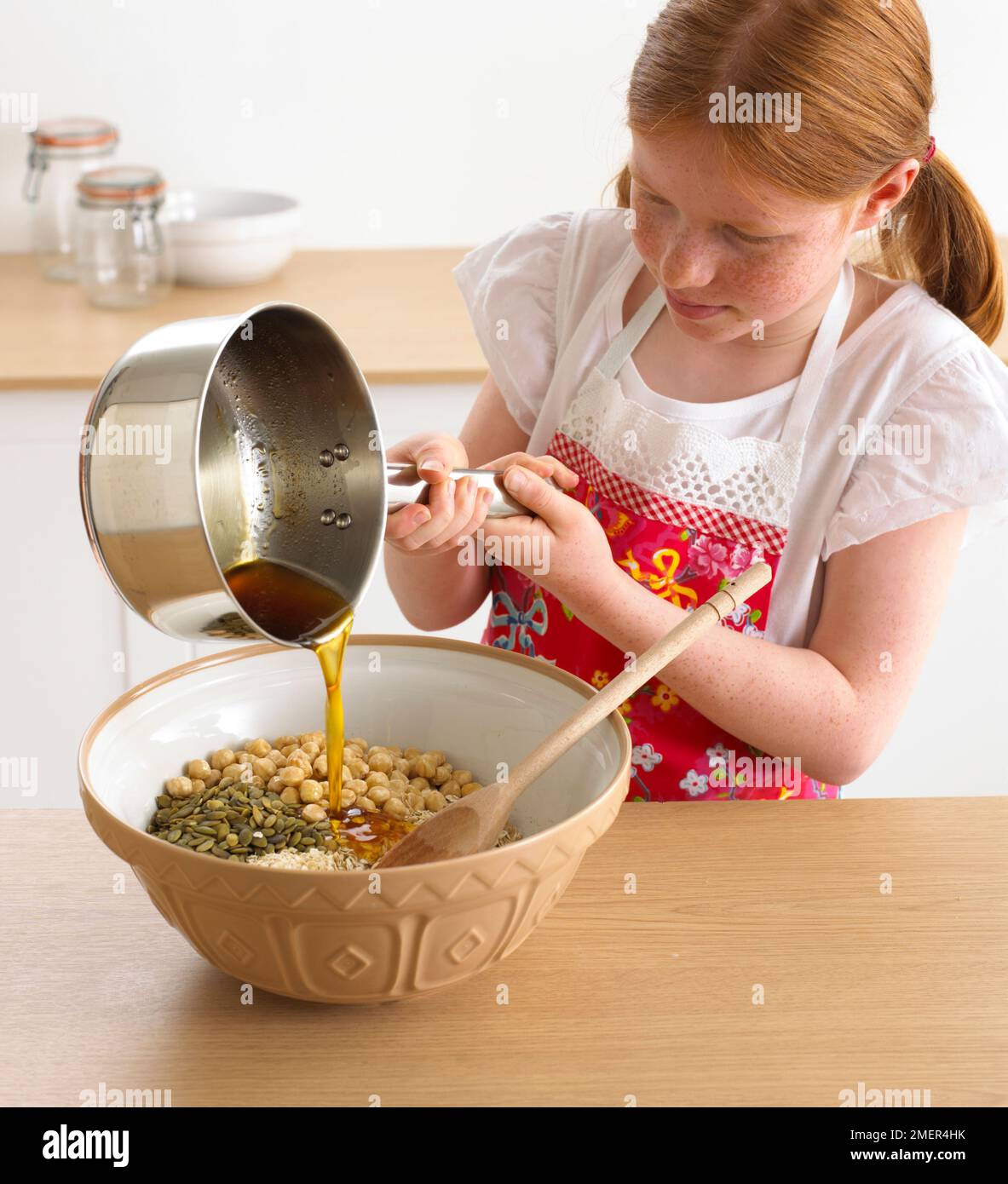 Girl pouring golden syrup and oil mixture into bowl of cereal, 9 years ...