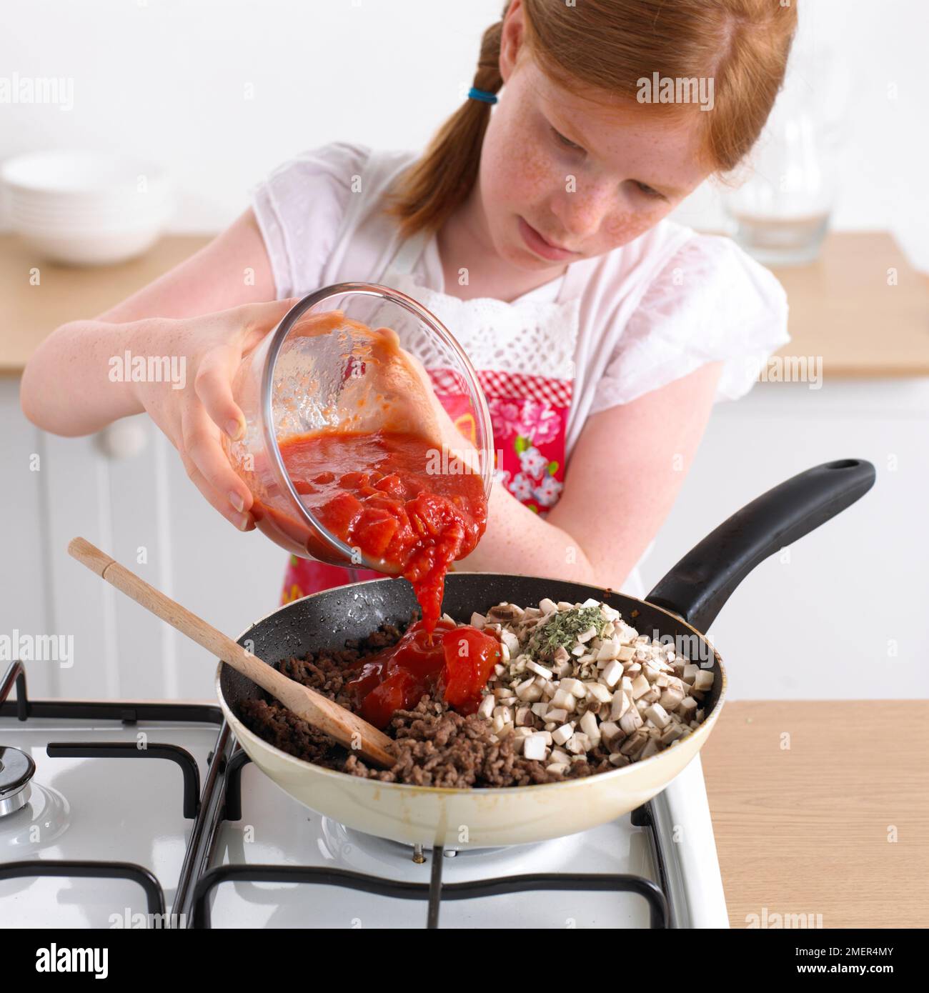 Girl adding chopped tomatoes to mushrooms, oregano and garlic, 9 years ...