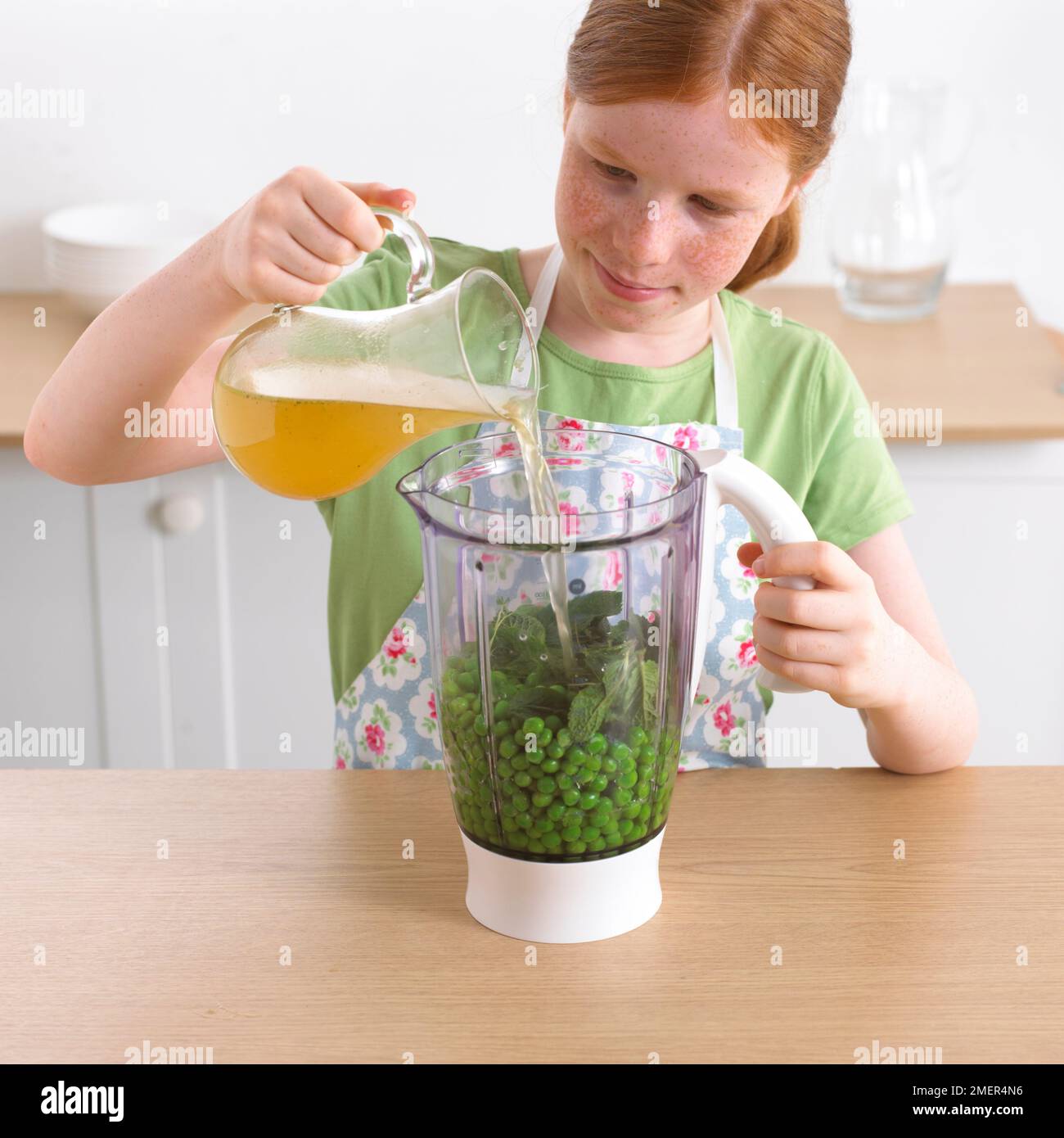 Making pea soup, Girl pouring vegetable stock to a blender of peas and ...