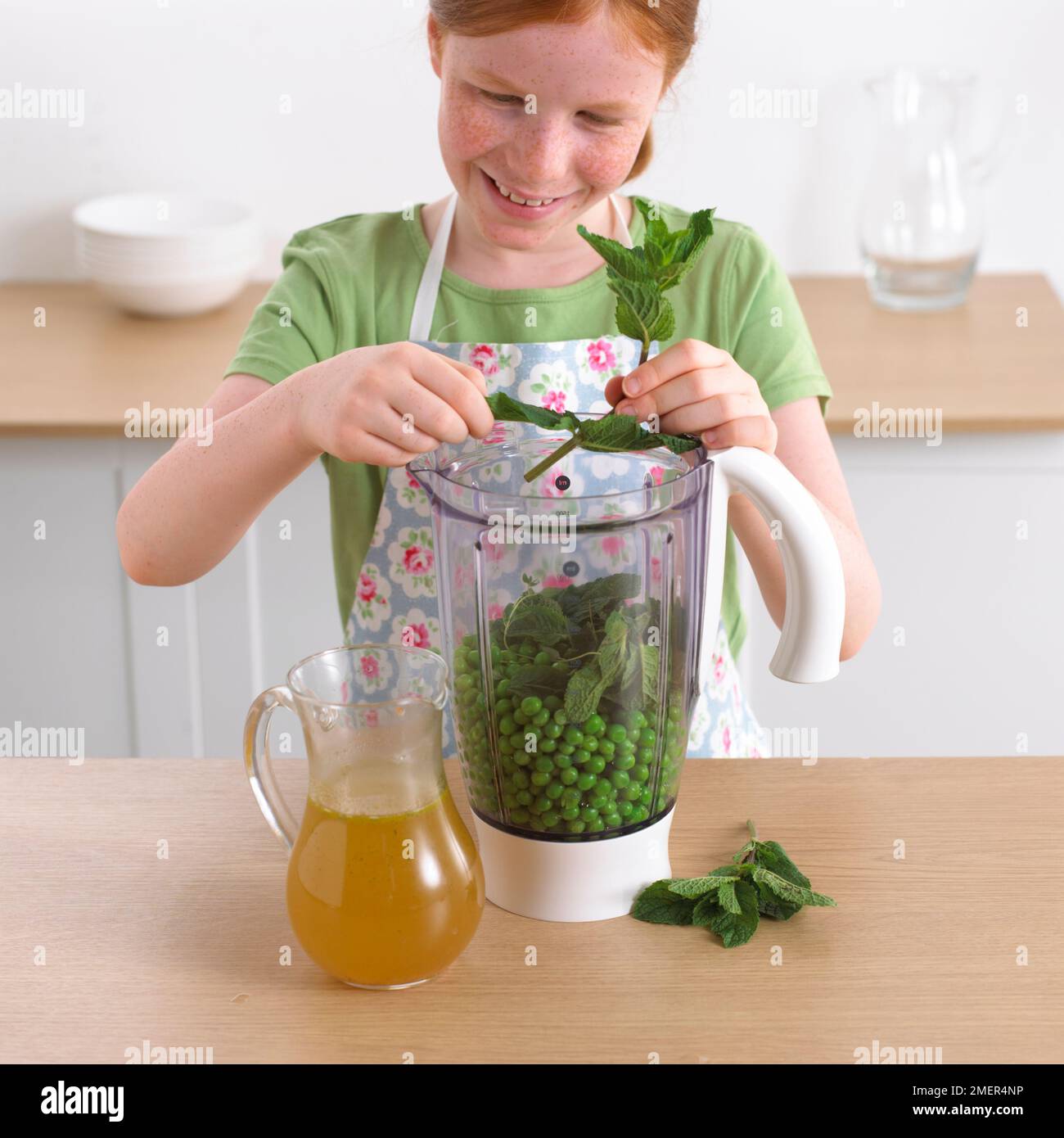 Making pea soup, Girl adding mint to a blender containg peas, jug of ...