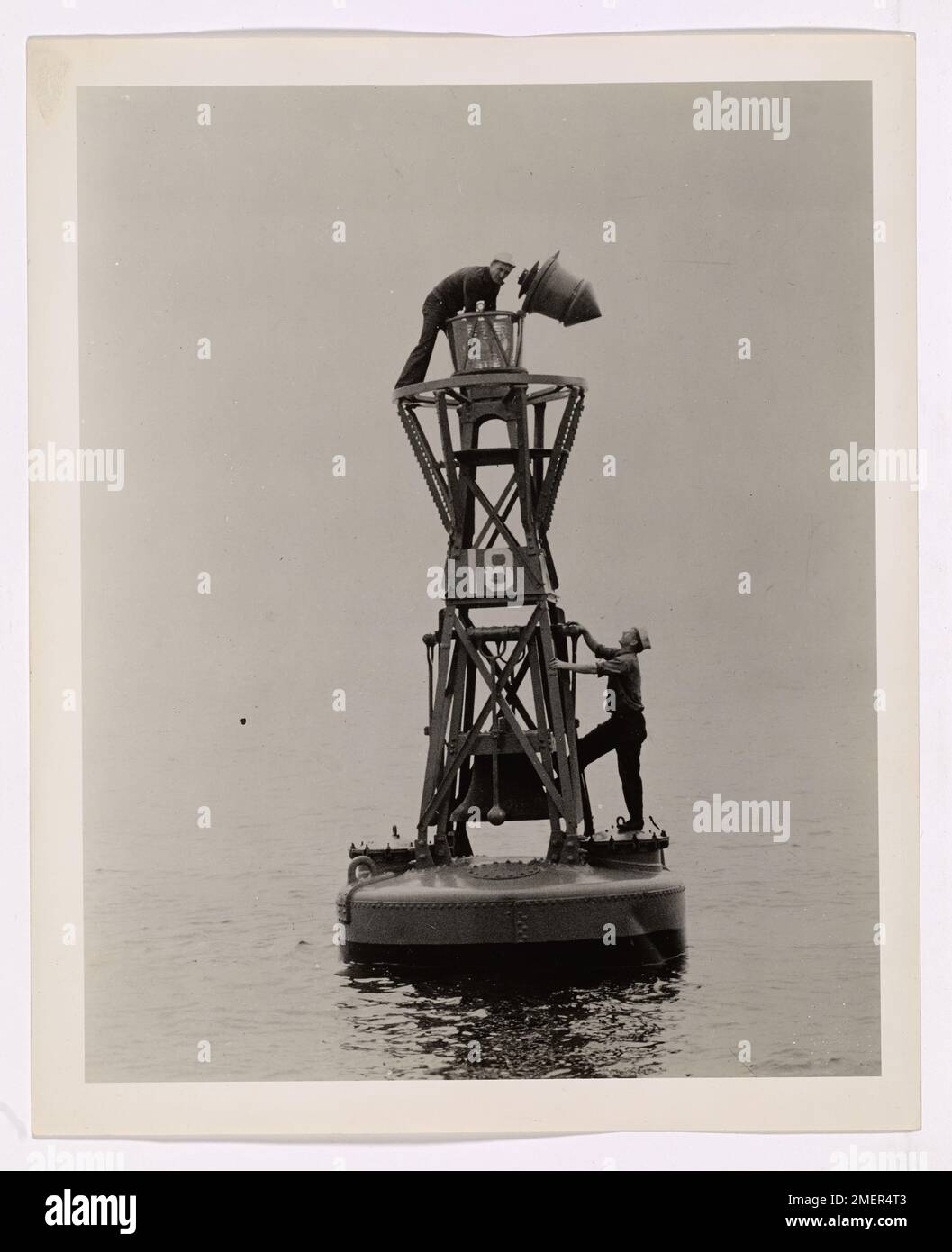 Two Coast Guardsmen perform maintenance on a numbered, lighted bell ...