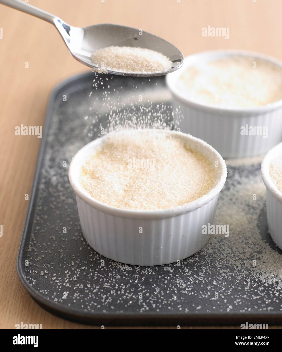 Sprinkling sugar on uncooked raspberry creme brulee Stock Photo - Alamy
