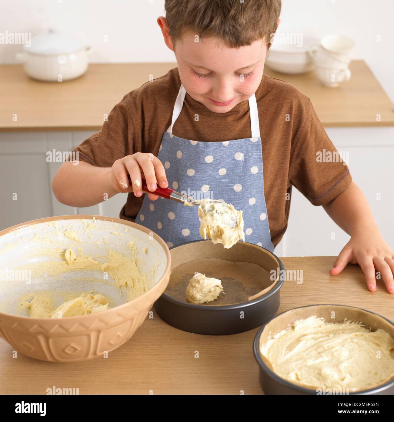 Boy putting sponge mixture into cake tins, 8 years Stock Photo - Alamy