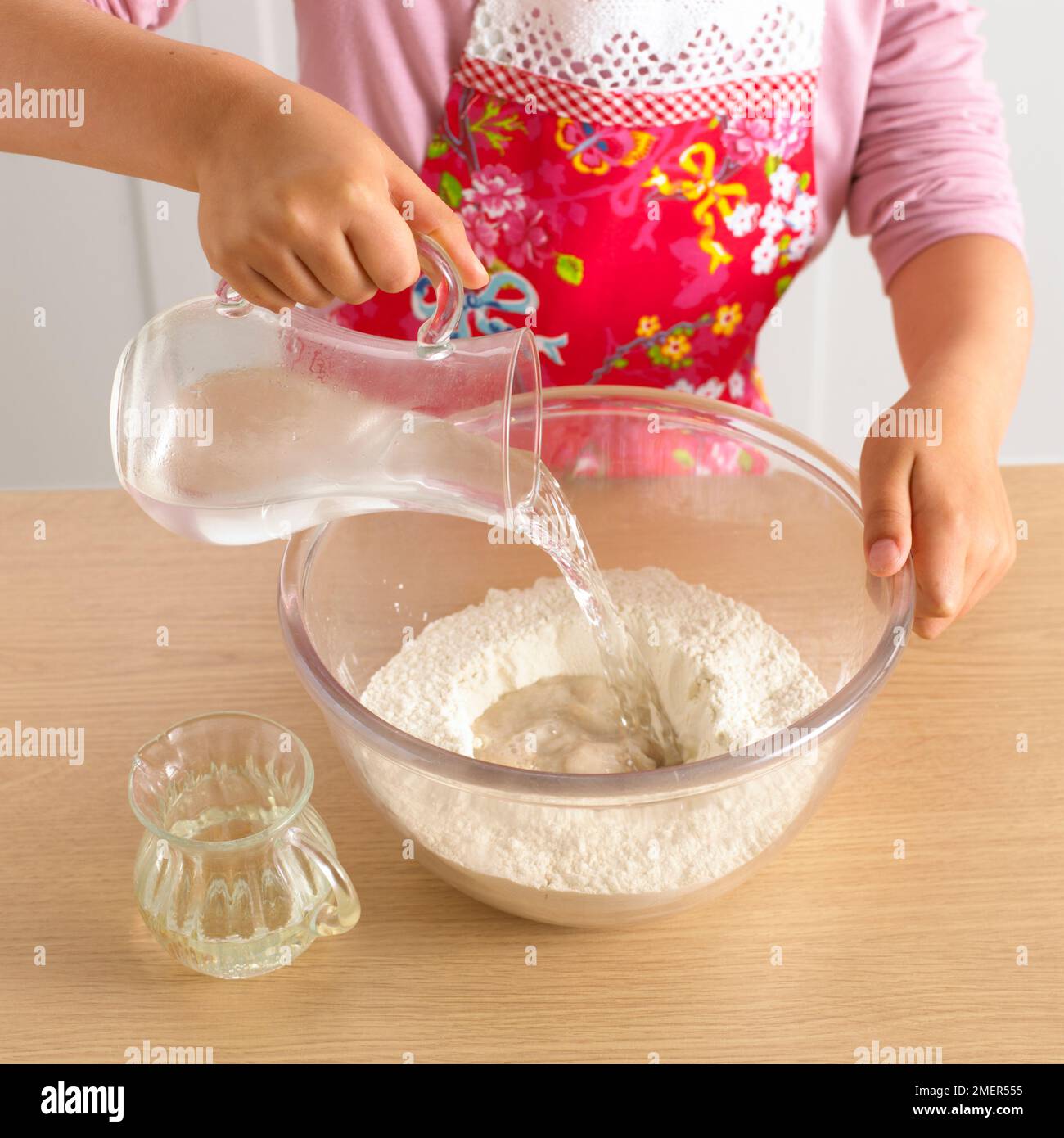 Girl pouring water into bowl of flour mixture, making pizza dough Stock ...