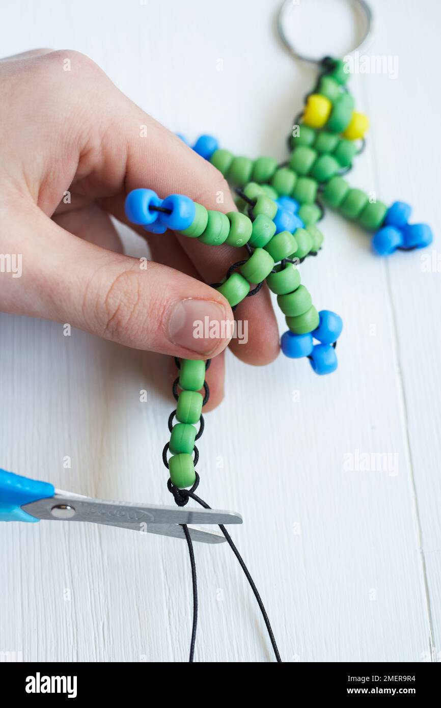 Making beaded lizard key ring, cutting off excess string with scissors ...