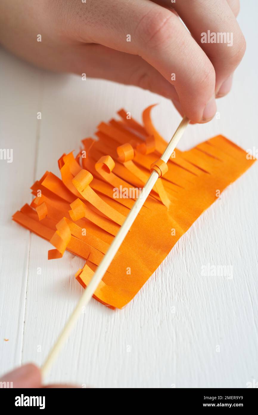 Cutting strands into folded orange paper and rolling, making hair for ...