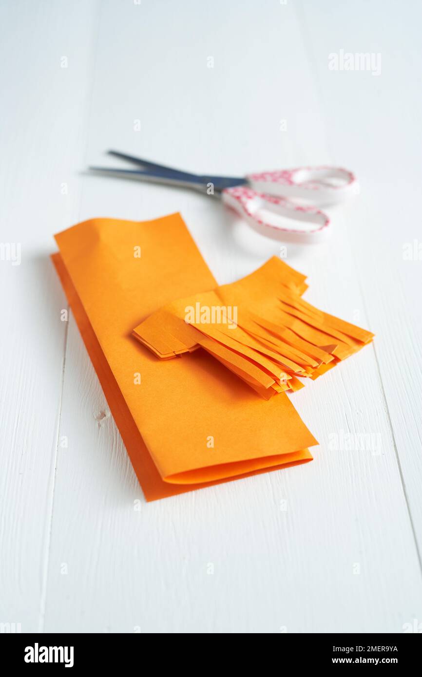 Cutting strands into folded orange paper, making hair for paper fairy ...
