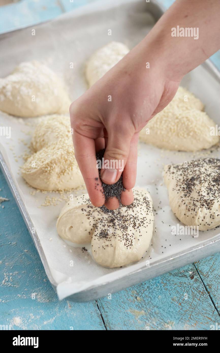 Sprinkling poppy seeds over heart shaped bread rolls Stock Photo - Alamy