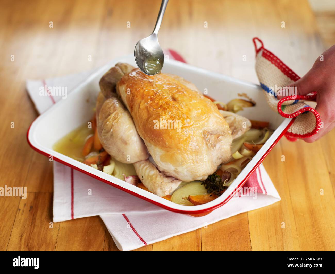 Roast chicken, pouring oil on whole semi-cooked chicken in baking dish ...