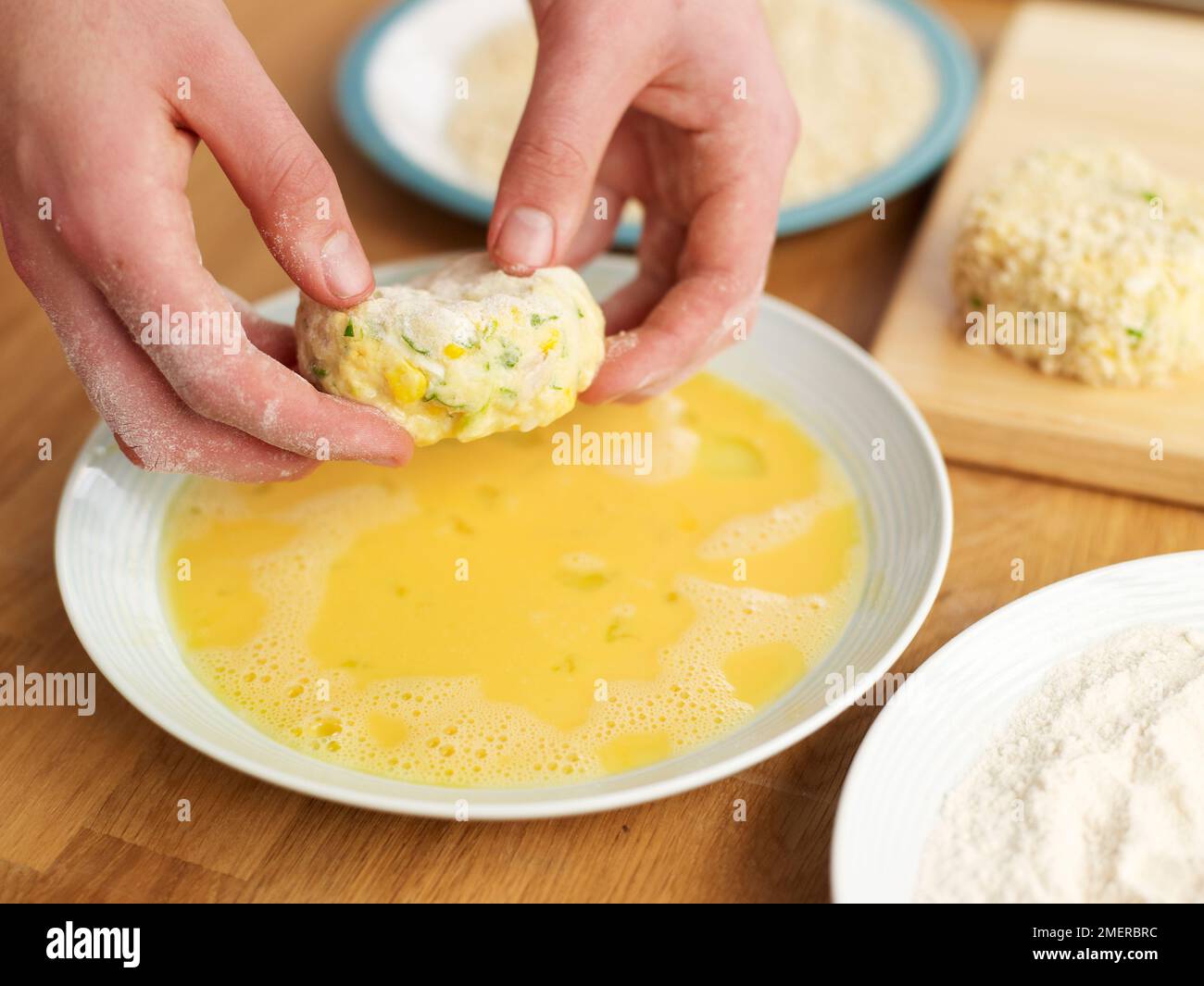 Dipping uncooked fish cakes in beaten egg Stock Photo - Alamy