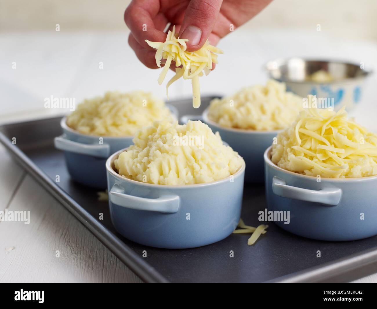 Making mashed potato pies, adding grated cheese on top of mash Stock ...