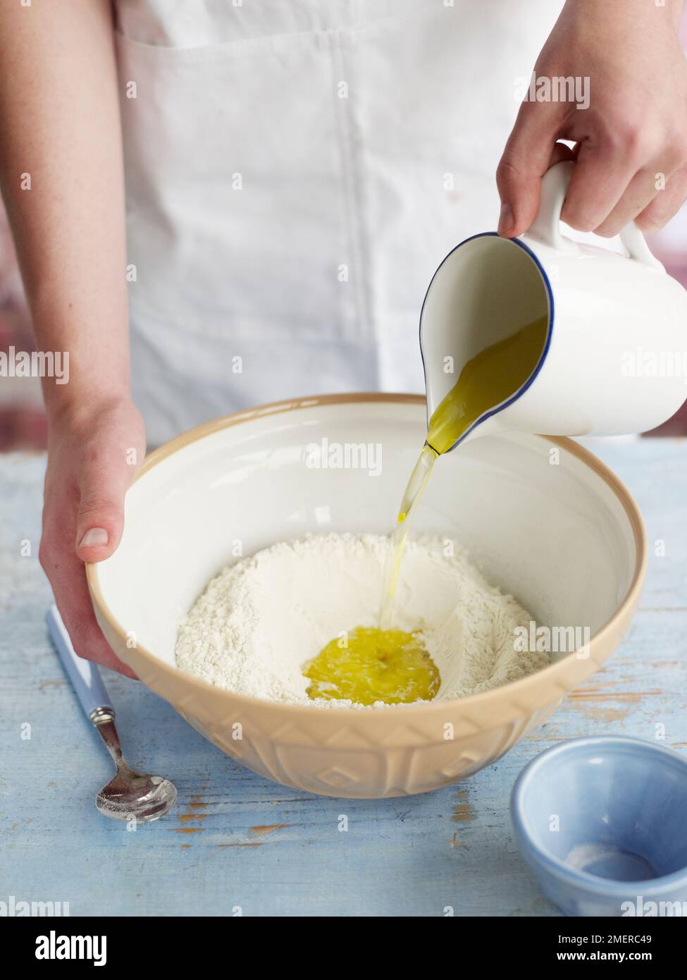Pouring olive oil and water into flour well, making focaccia bread ...