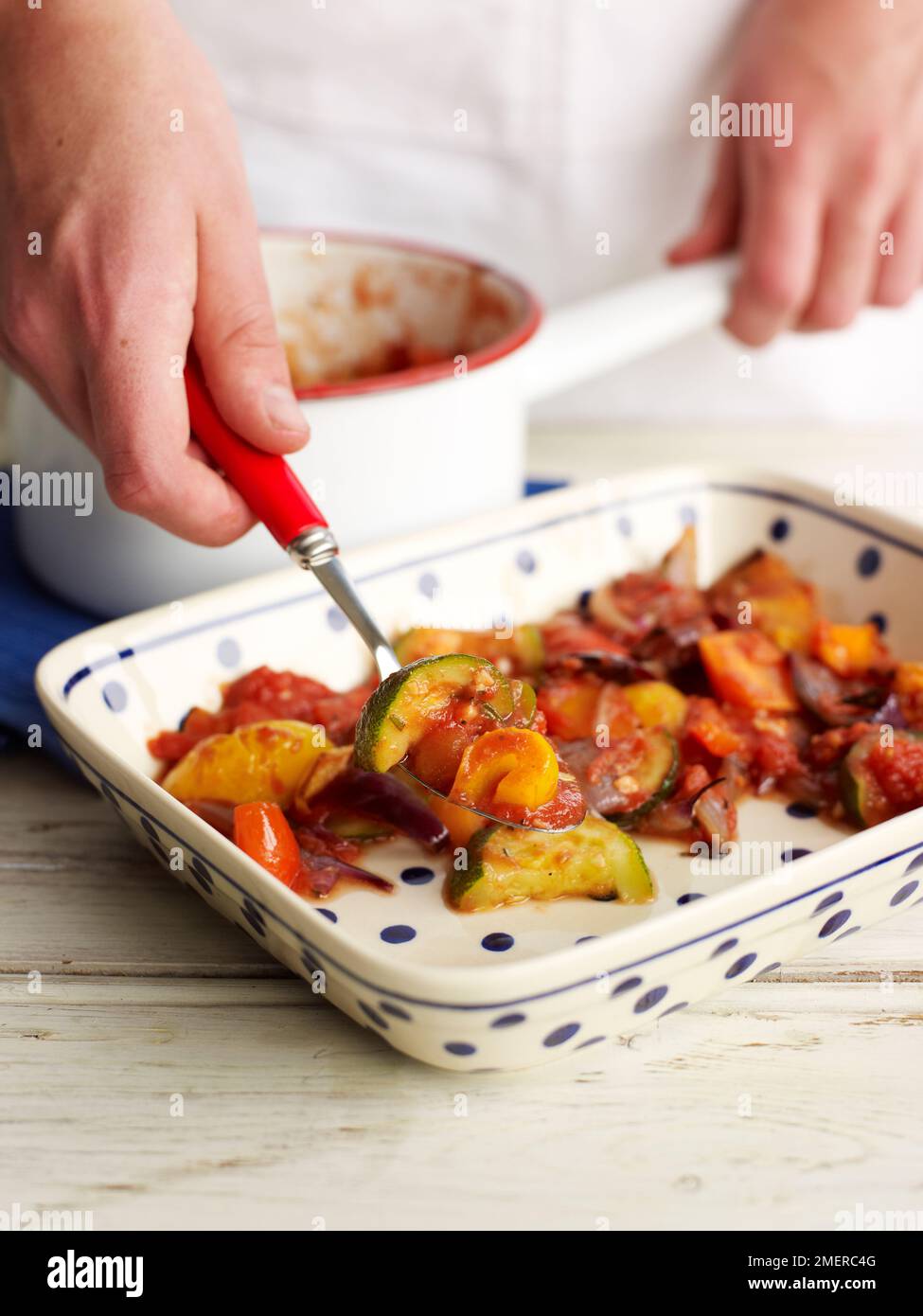 Spooning vegetables into baking tray or dish, bottom layer for ...