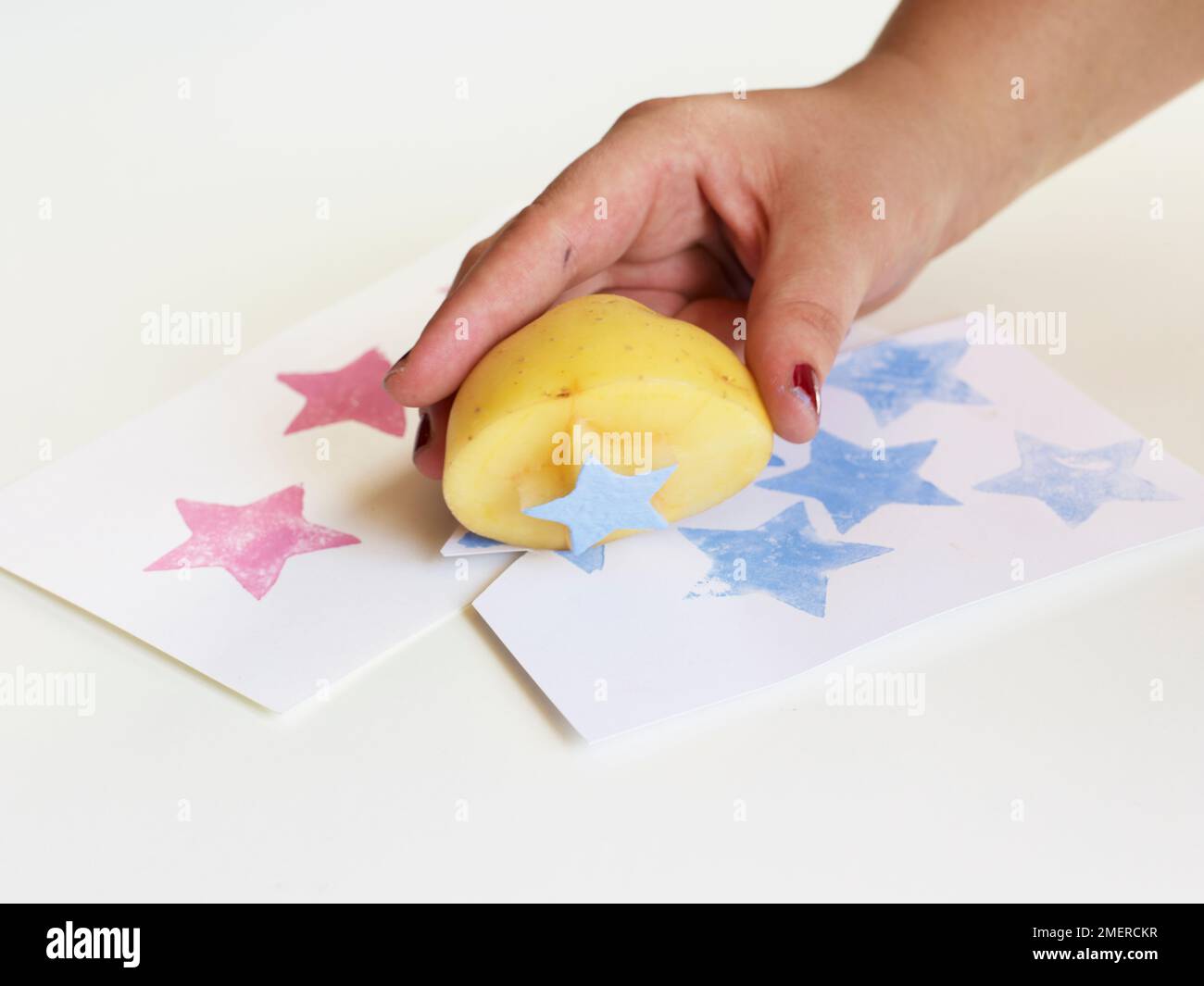 Using potato stamp to print blue and pink stars on white paper Stock ...