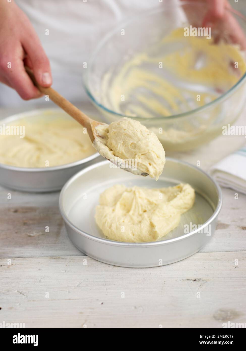 Dividing sponge mixture between two greased cake tins, making Victoria ...