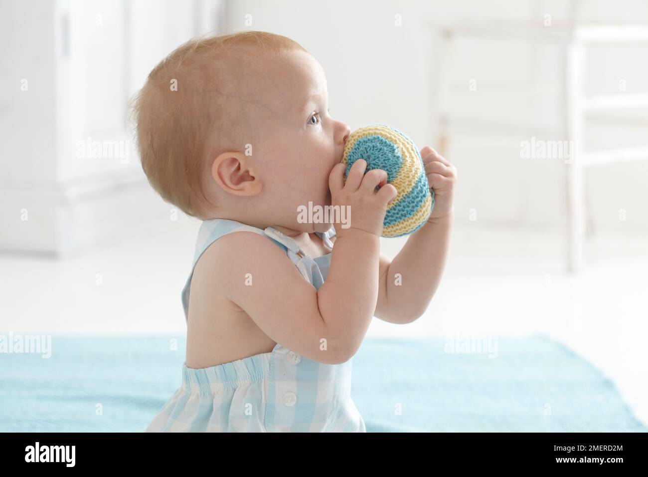 Baby girl, chewing knitted soft toy ball, 9 months Stock Photo - Alamy