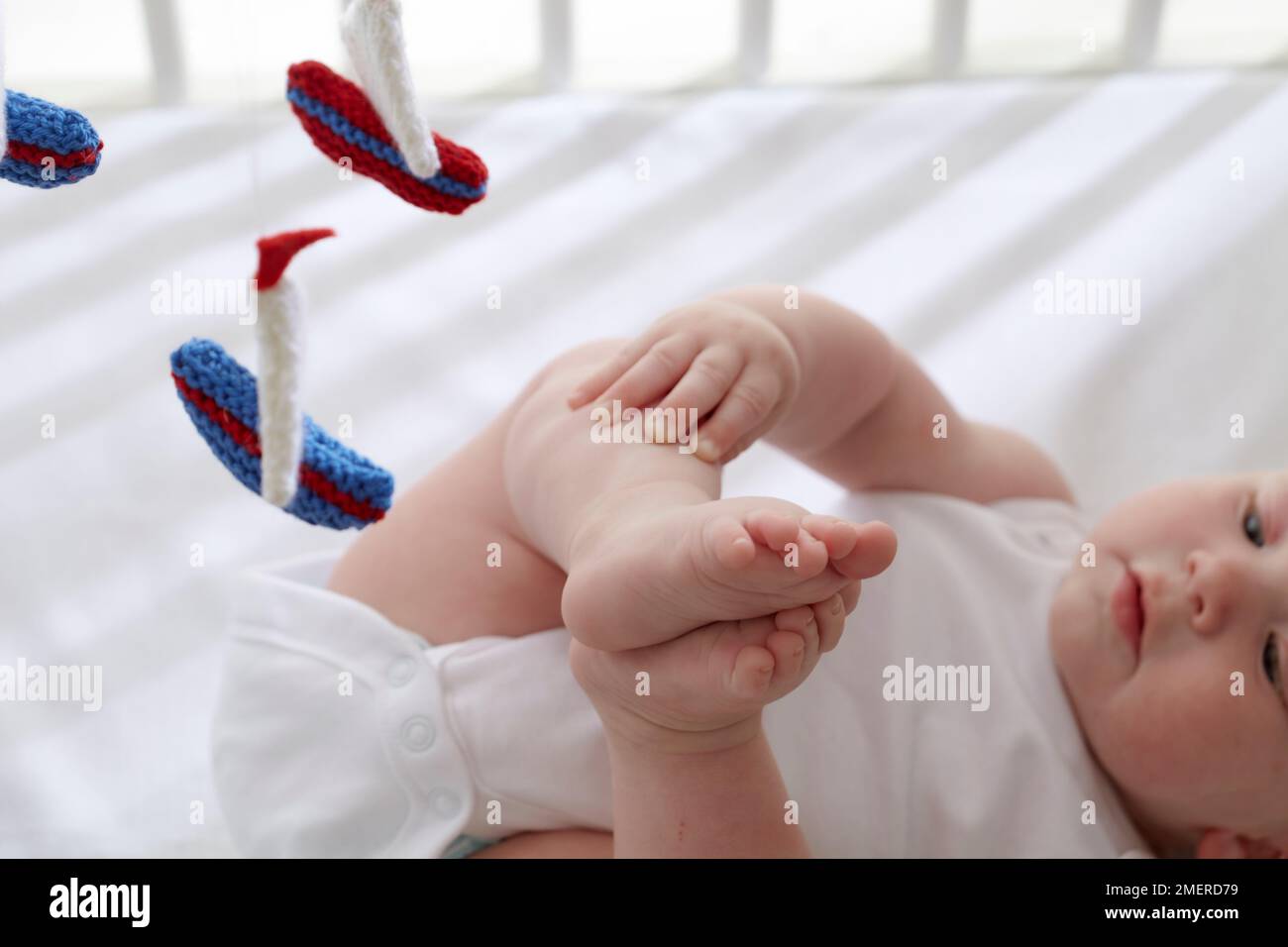 Baby boy lying down reaching up to knitted sailing boat mobile, 5 ...
