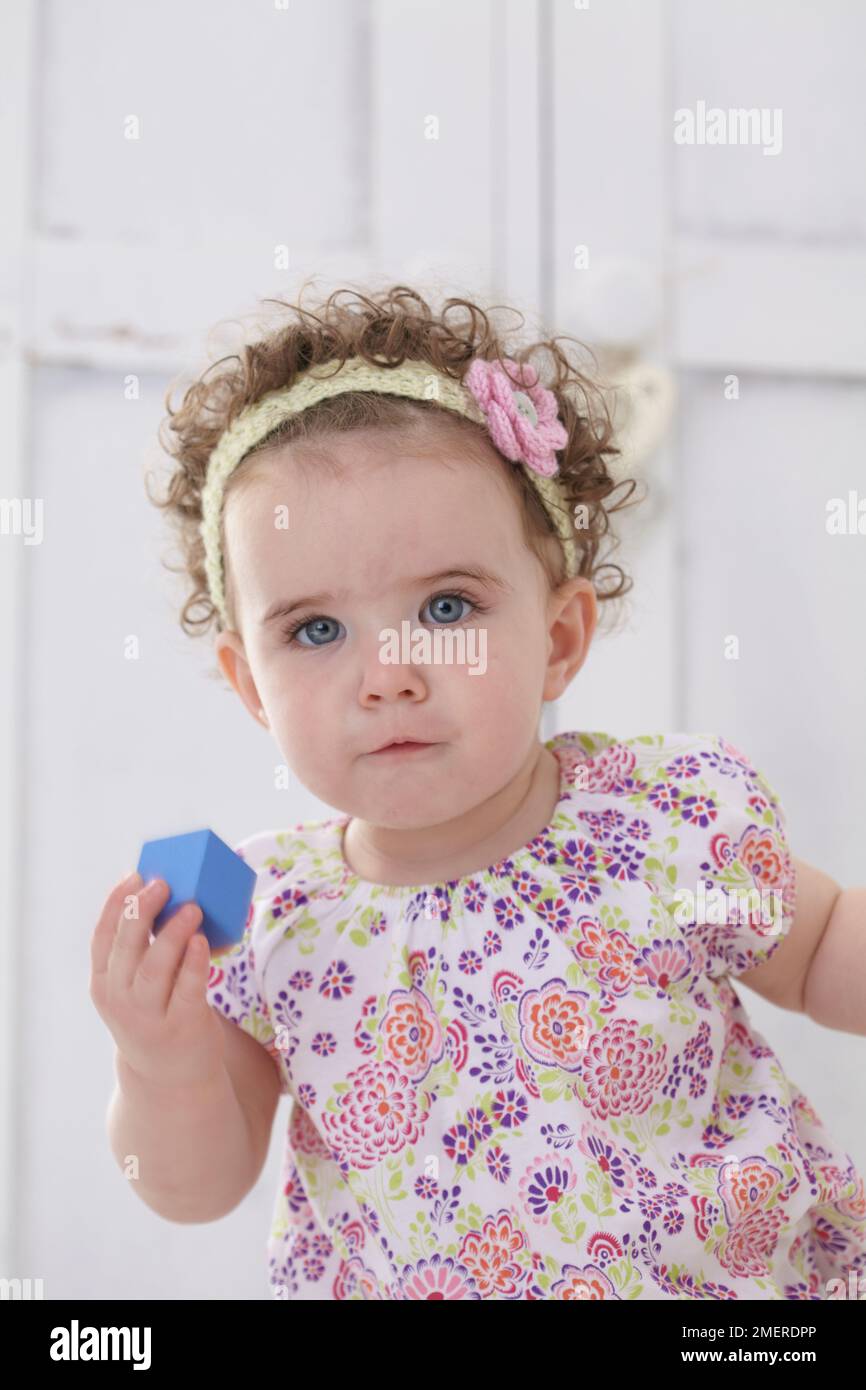 Baby girl sitting wearing knitted headband and holding building block ...