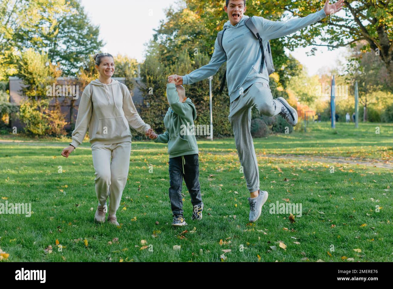 a family mom and 2 sons are having fun, running in the park and jumping ...