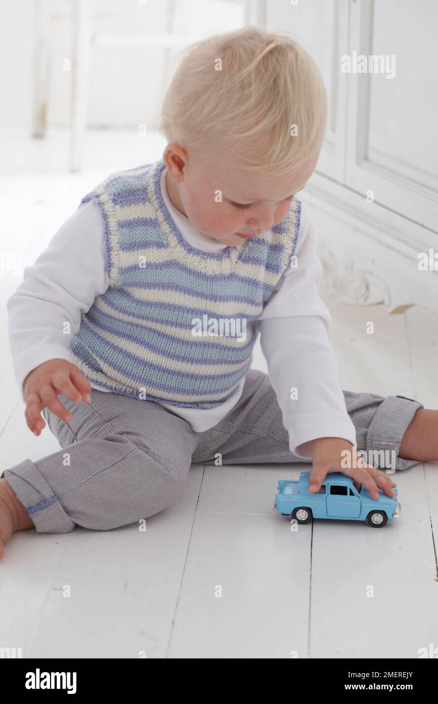 Baby boy sitting on floor playing with blue car, 14 months Stock Photo ...