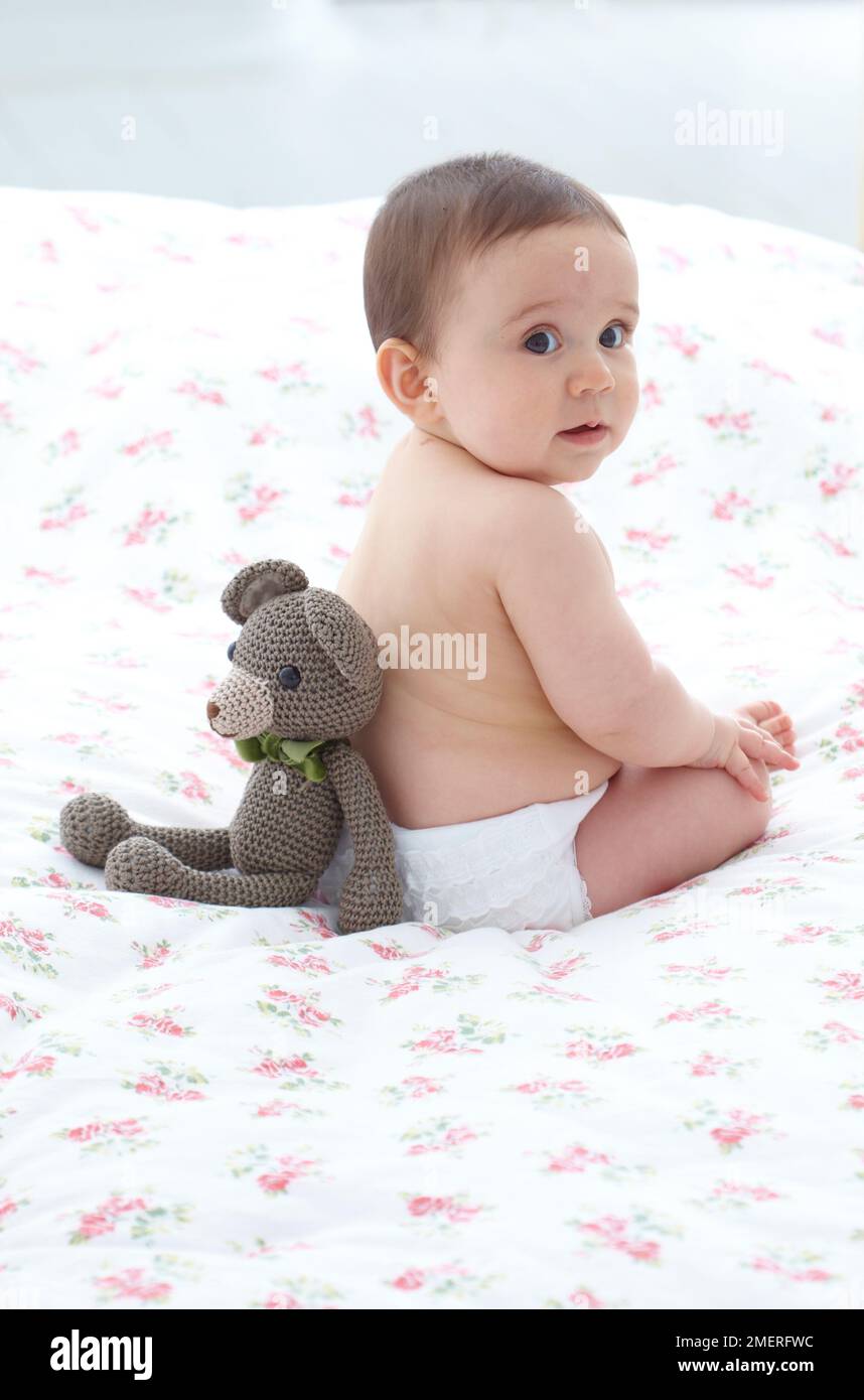 Baby boy sitting back to back with a crocheted bear, 6.5 months Stock ...