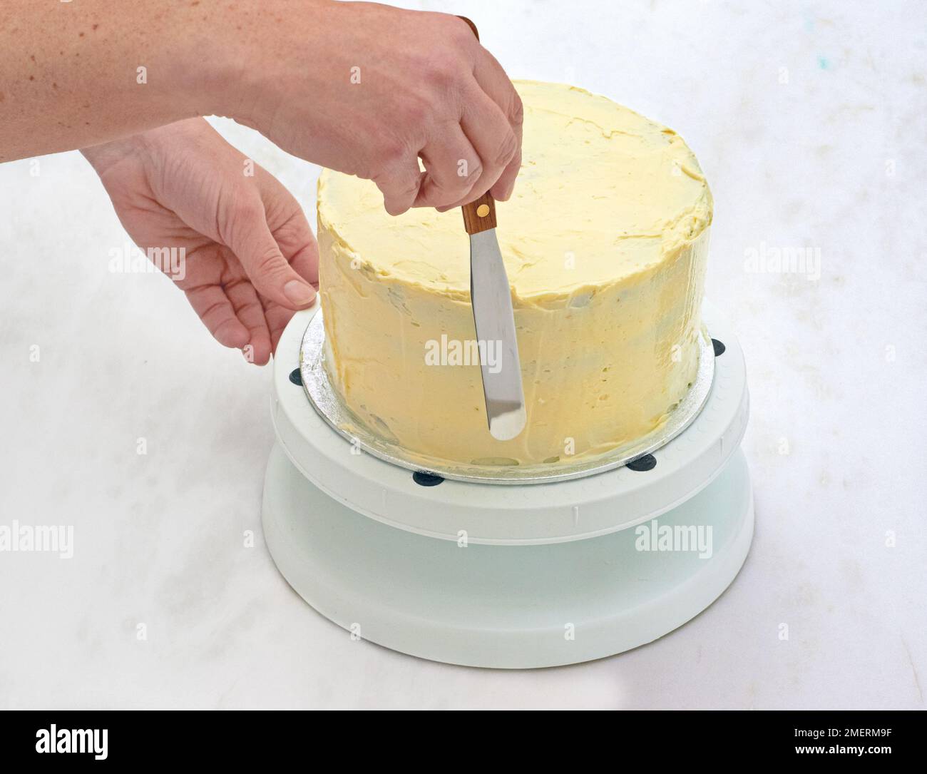 Spreading crumb coat of icing on cake Stock Photo - Alamy