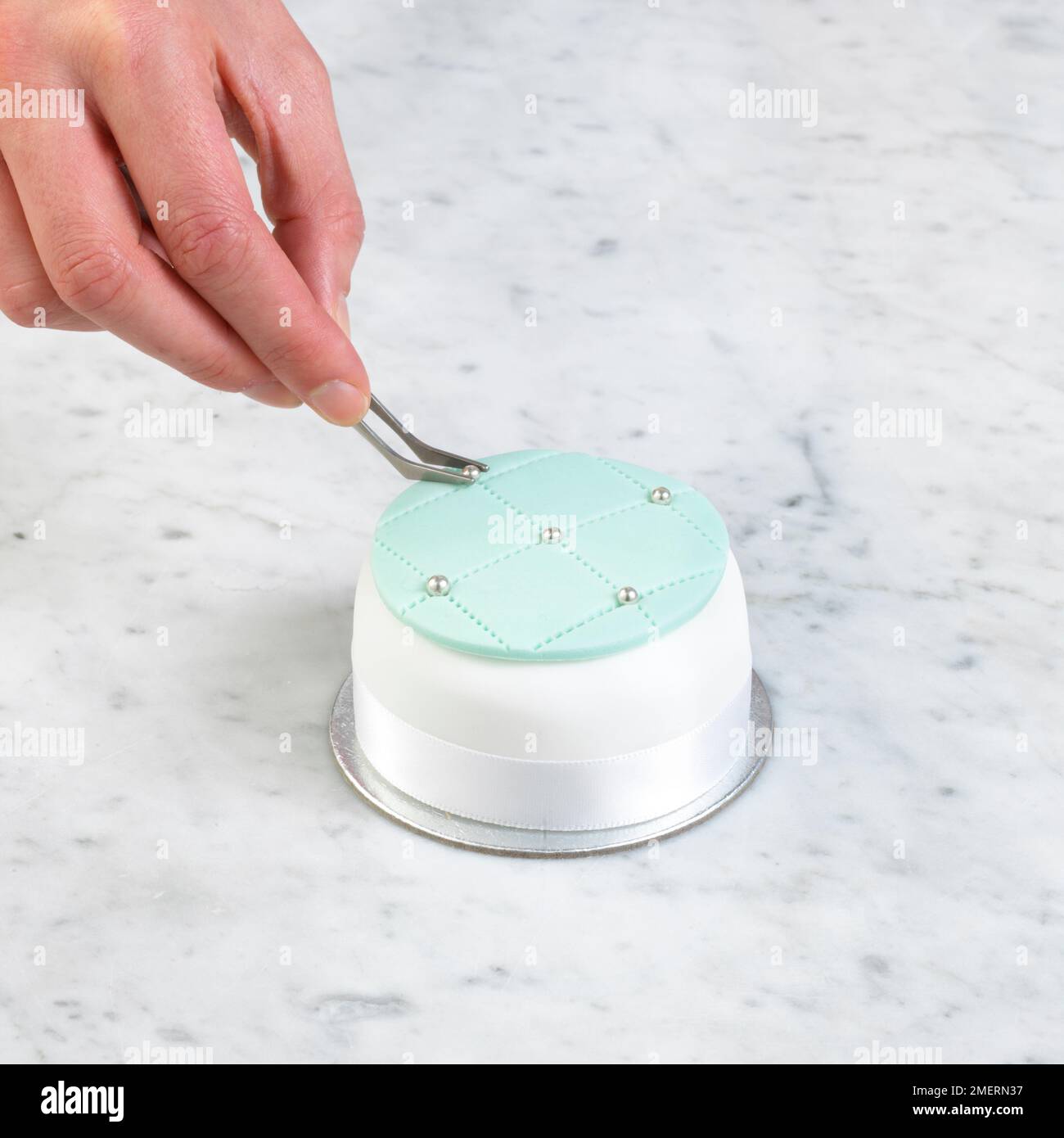 Placing edible silver bead on smooth iced cake using tweezers Stock ...