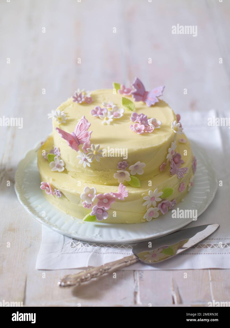 Two-tiered iced cake decorated with flowers and butterflies made of ...