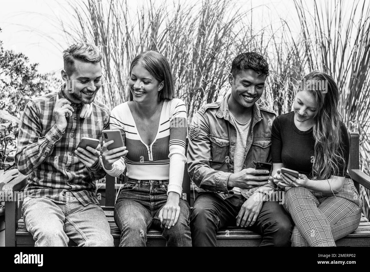 Multicultural friends having fun together looking at their smartphones ...