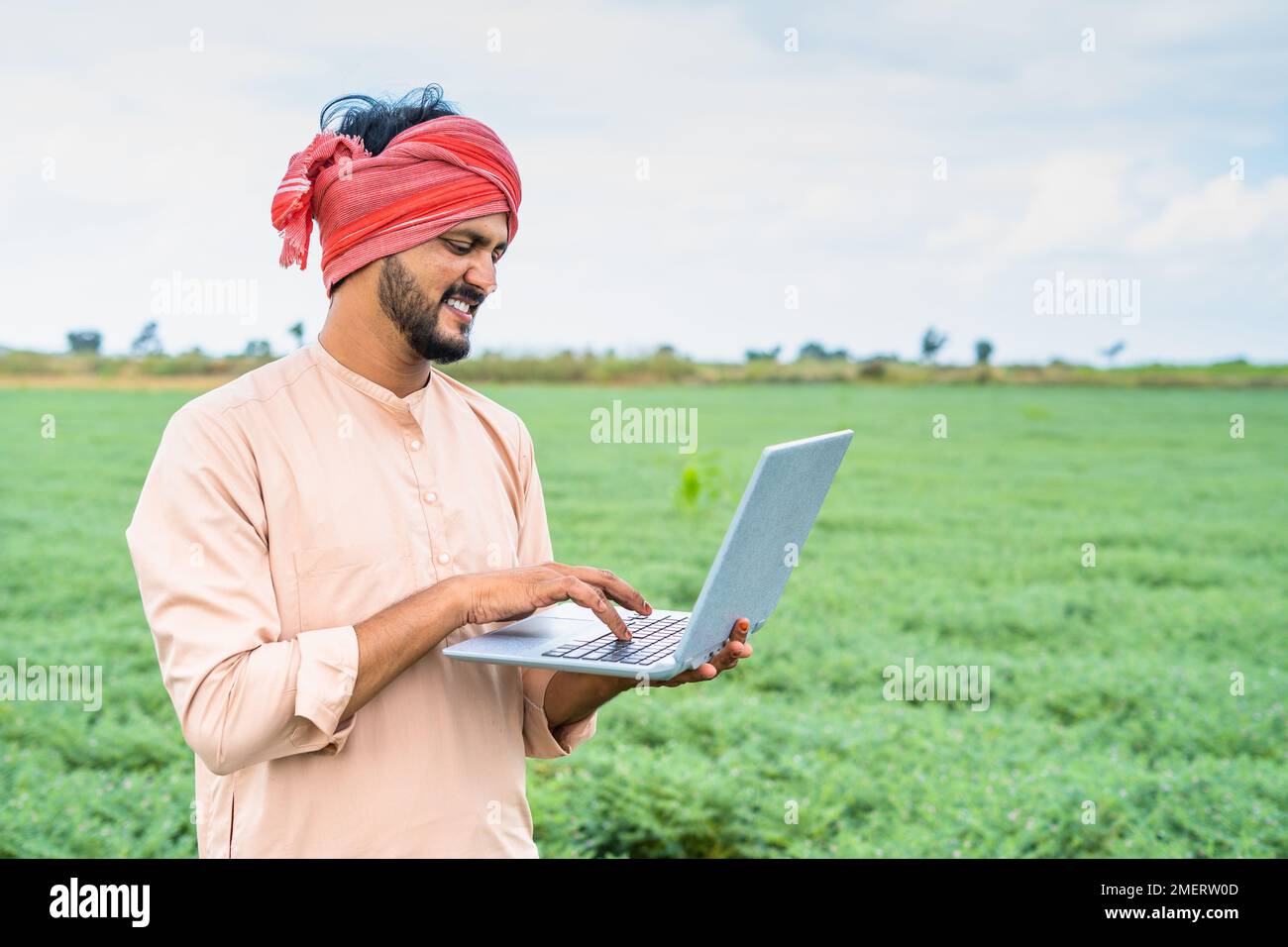Young indian farmer busy wrking on laptop while sitting at agricultural ...