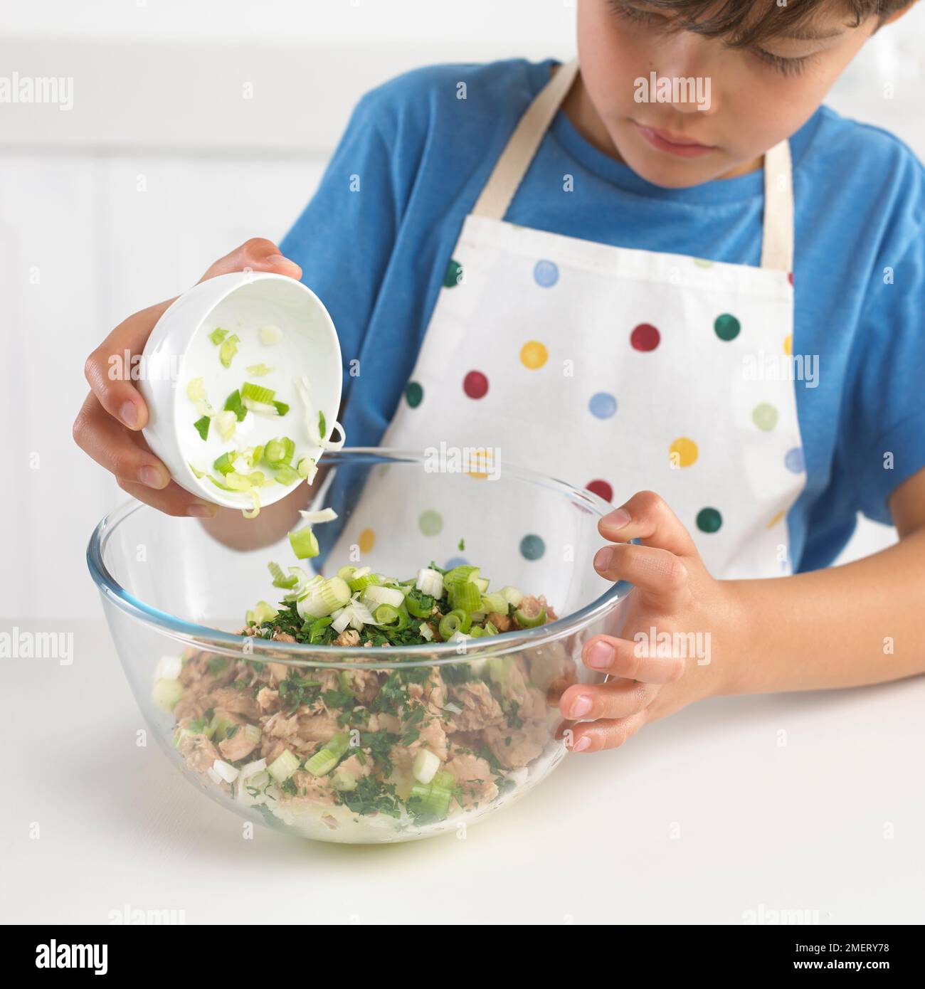 Making fishcakes, Pouring chopped spring onions to bowl of potato and ...