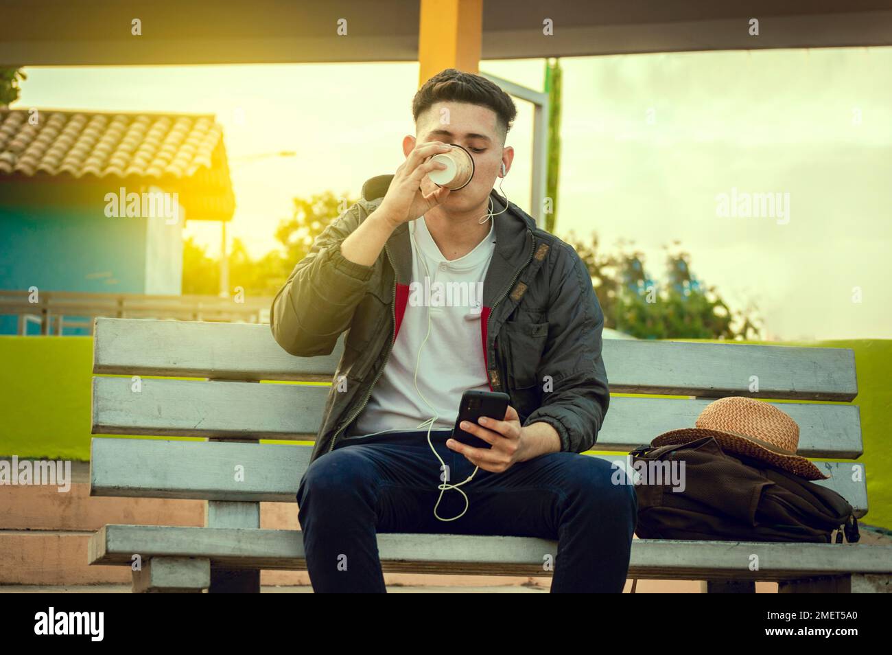 Relaxed attractive boy listening to music on a bench, boy sitting on a ...