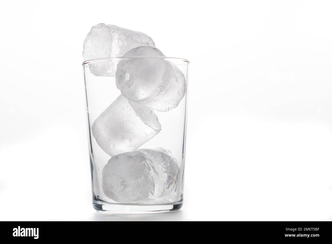 Glass tumbler with ice cubes foreground white background and copy space ...
