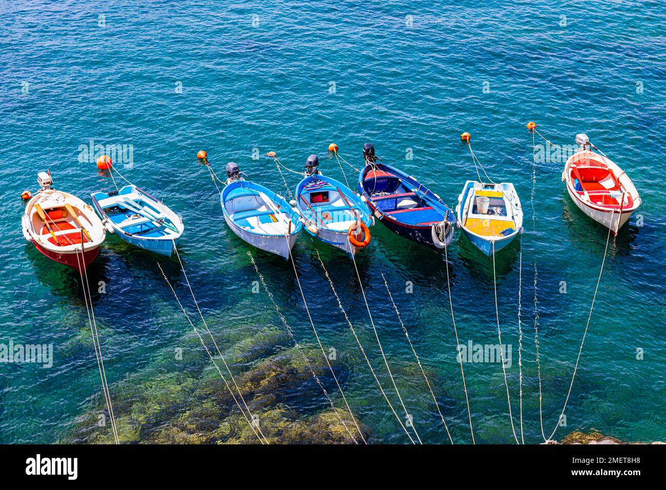 Colourful fishing boats attached to the rock lie in the turquoise water ...