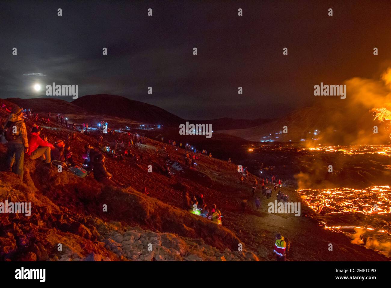 People watch as lava flows from an eruption of a volcano on the ...