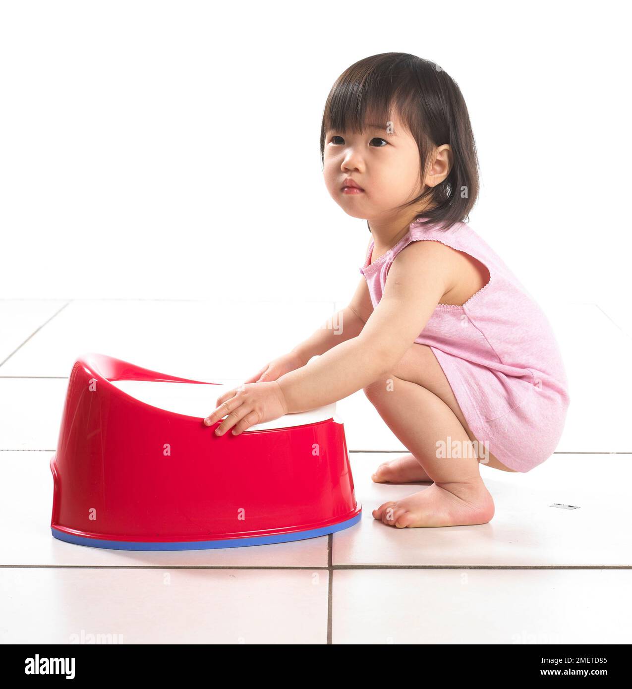 Girl crouching wearing pink vest holding a red potty, 20 months Stock Photo - Alamy