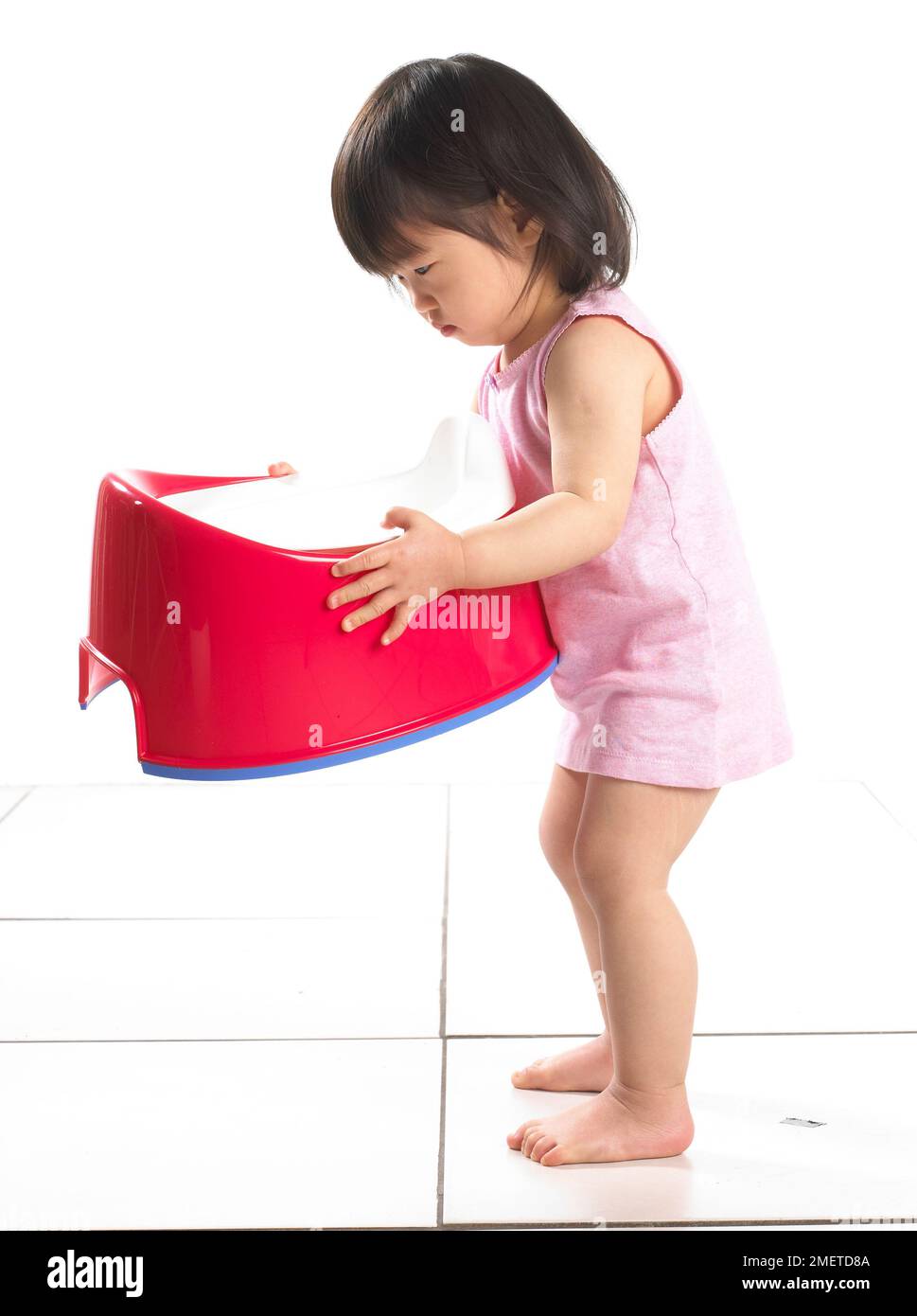 Girl standing wearing pink vest holding a red potty, 20 months Stock Photo - Alamy