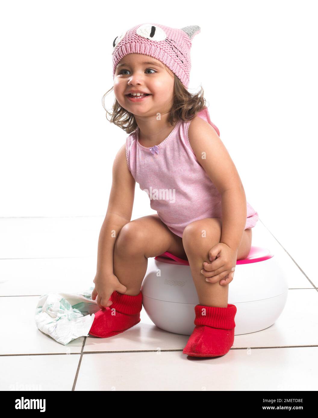 Girl wearing pink vest and pink wool hat, red slippers sitting on white potty holding nappy, 20 ...