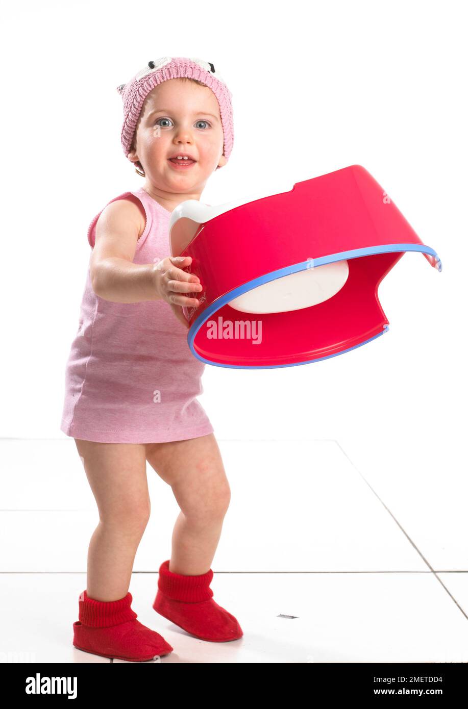Girl wearing red socks, pink top and pink wool hat holding red potty ...