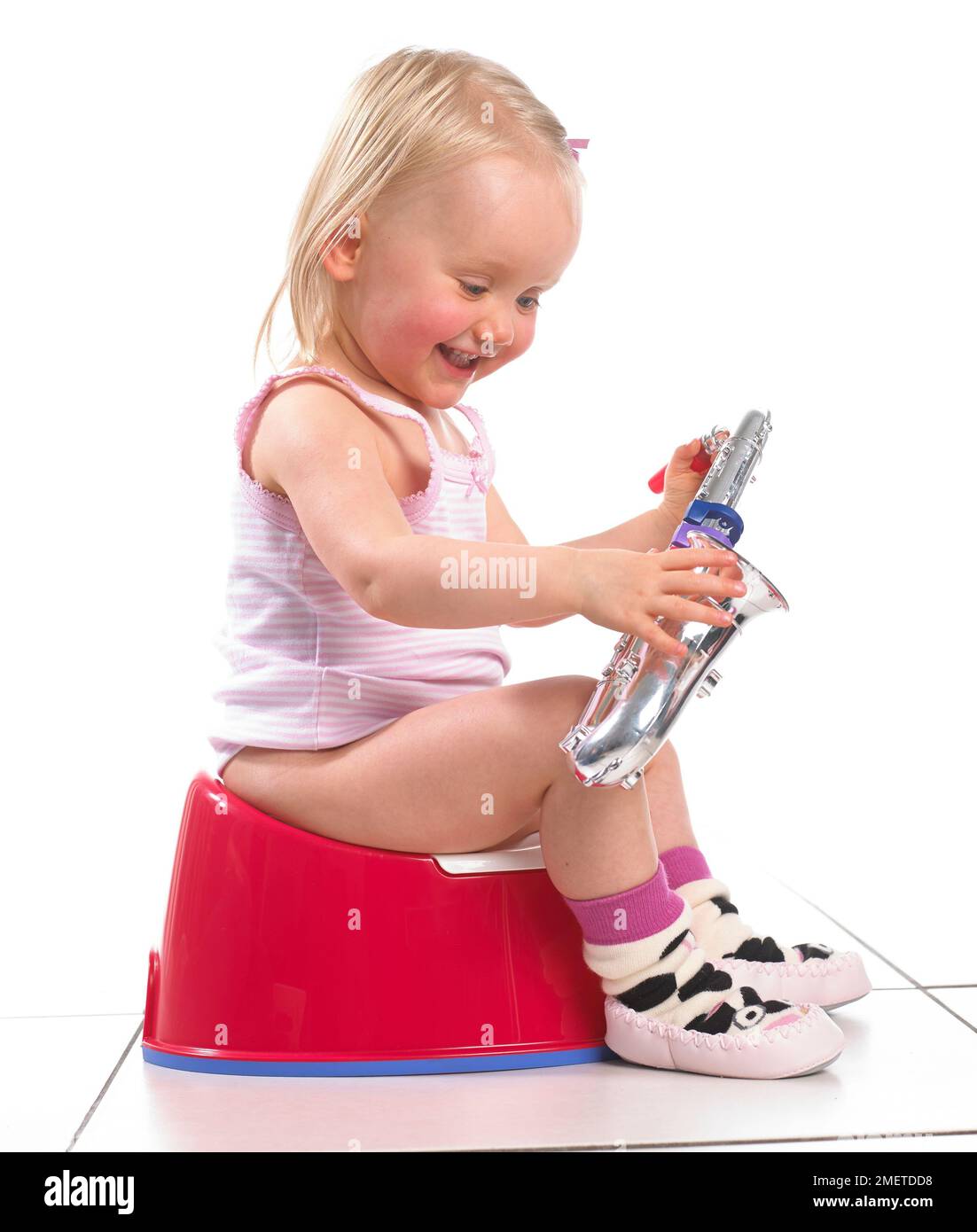 Girl Wearing Vest And Slippers Sitting On A Red Potty Playing With A