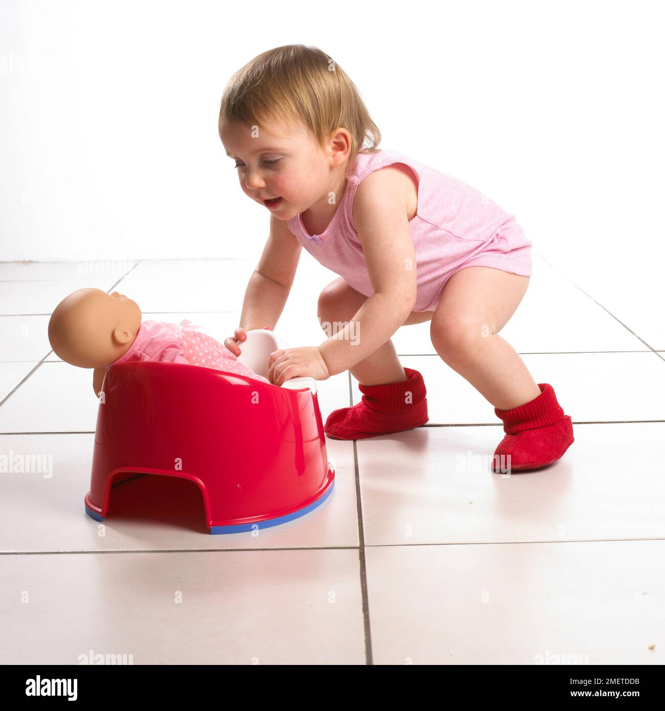 Girl crouching while putting doll in red potty, 19 months Stock Photo ...