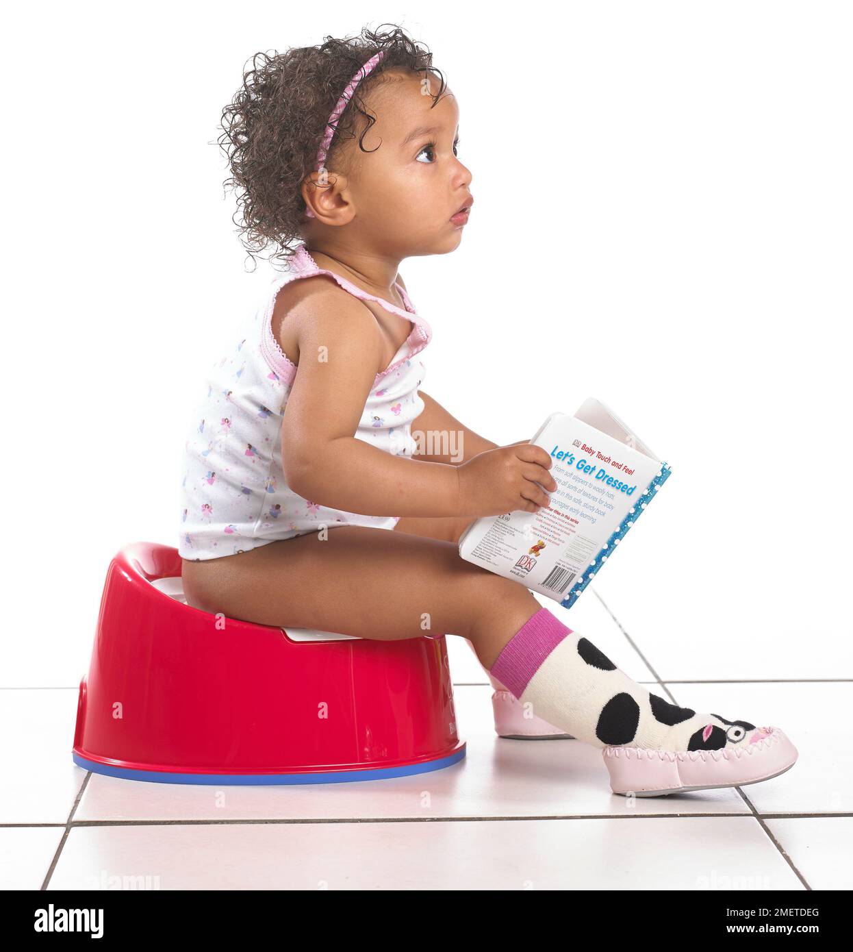 Girl wearing vest and slippers sitting on red potty reading a book, 16 months Stock Photo - Alamy