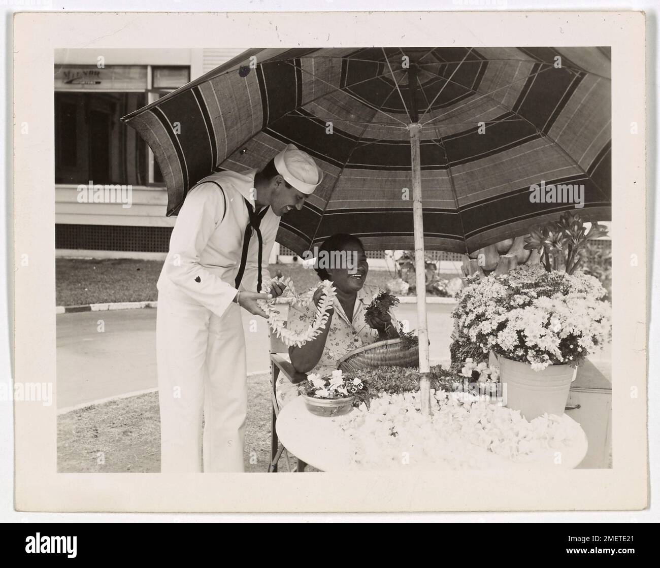Actor Cesar Romero is photographed with a woman making flower garlands ...