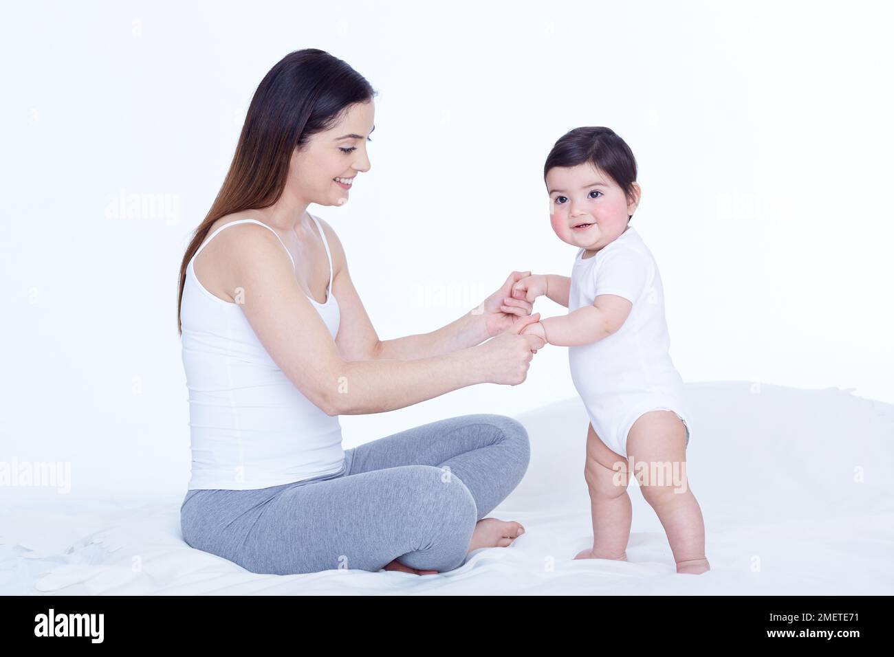 Mother sitting on bed, holding hands of baby girl (40 weeks) who is ...