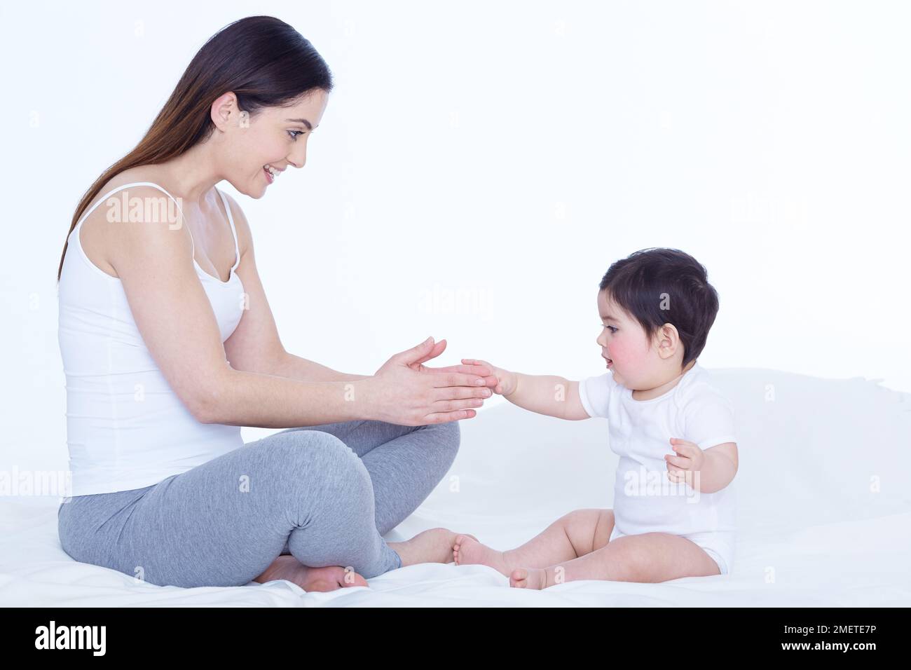 Baby girl (40 weeks) and mother sitting on bed, baby girl is touching ...